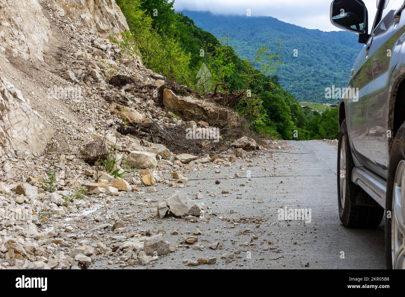 Limestone rockfall and landslide fallen on a tarmac road with car ...