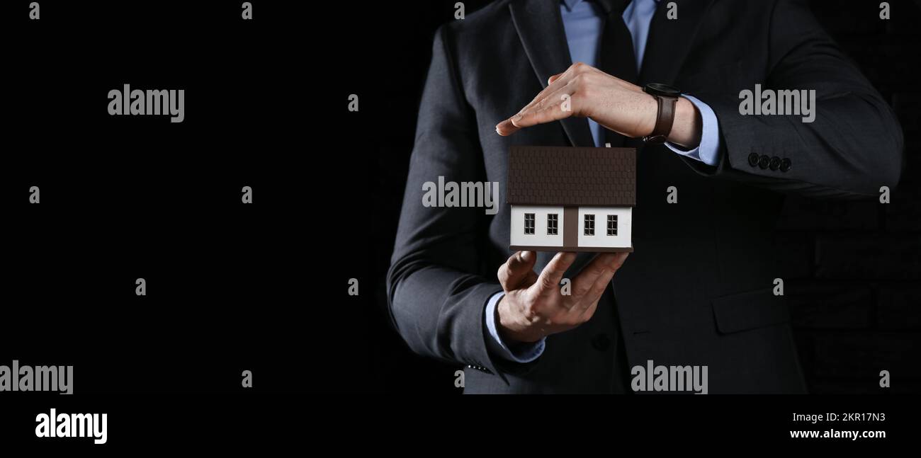 Insurance agent with model of house on dark background with space for ...