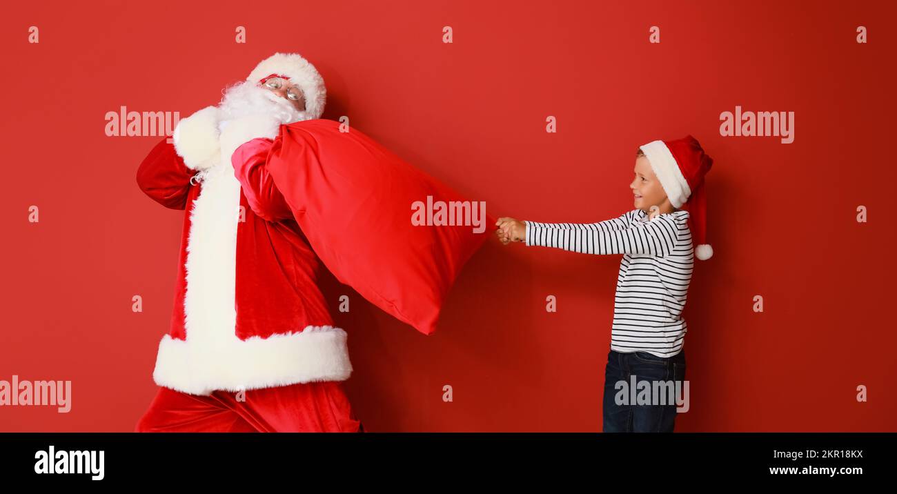 Little boy trying to take bag with gifts from Santa Claus against red ...