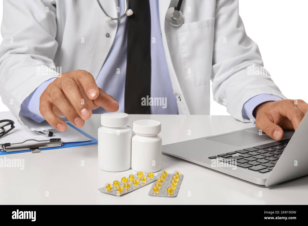 Male doctor with vitamins using laptop at table on white background ...