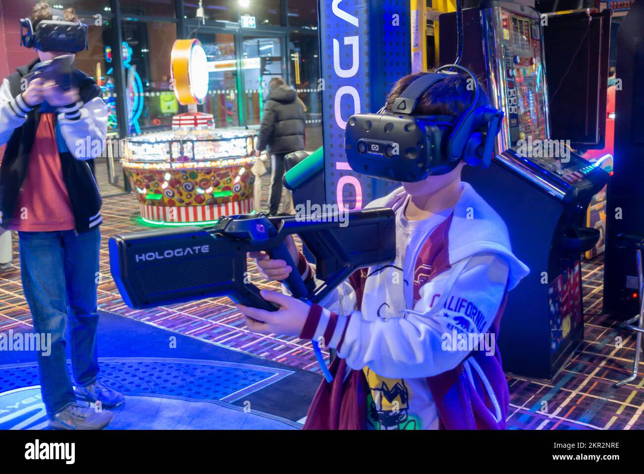 A boy playing a virtual reality video game in an arcade, holding a gun ...
