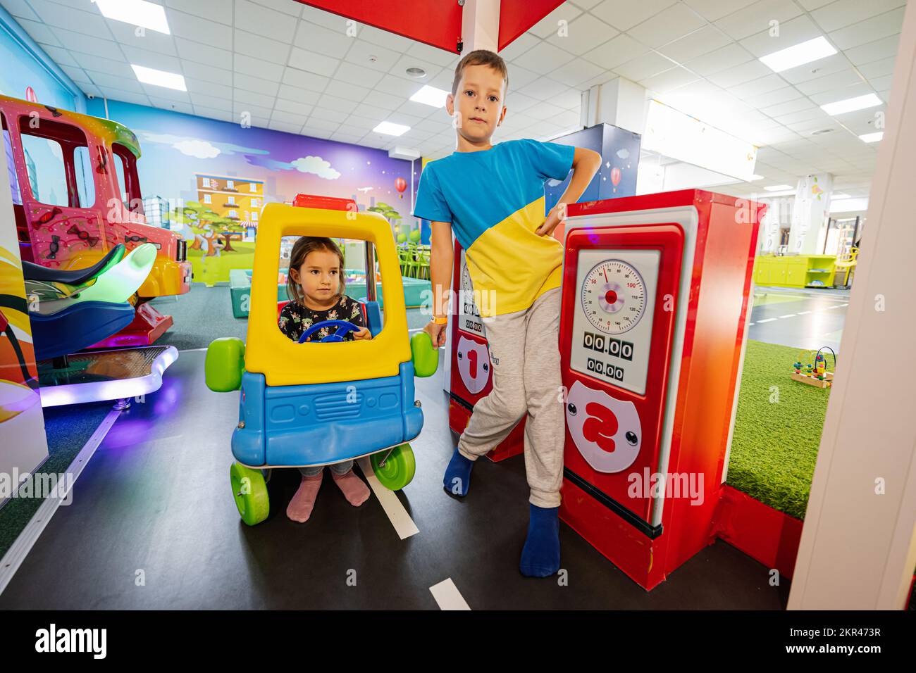 Brother with sister playing at indoor play center playground in toy car ...