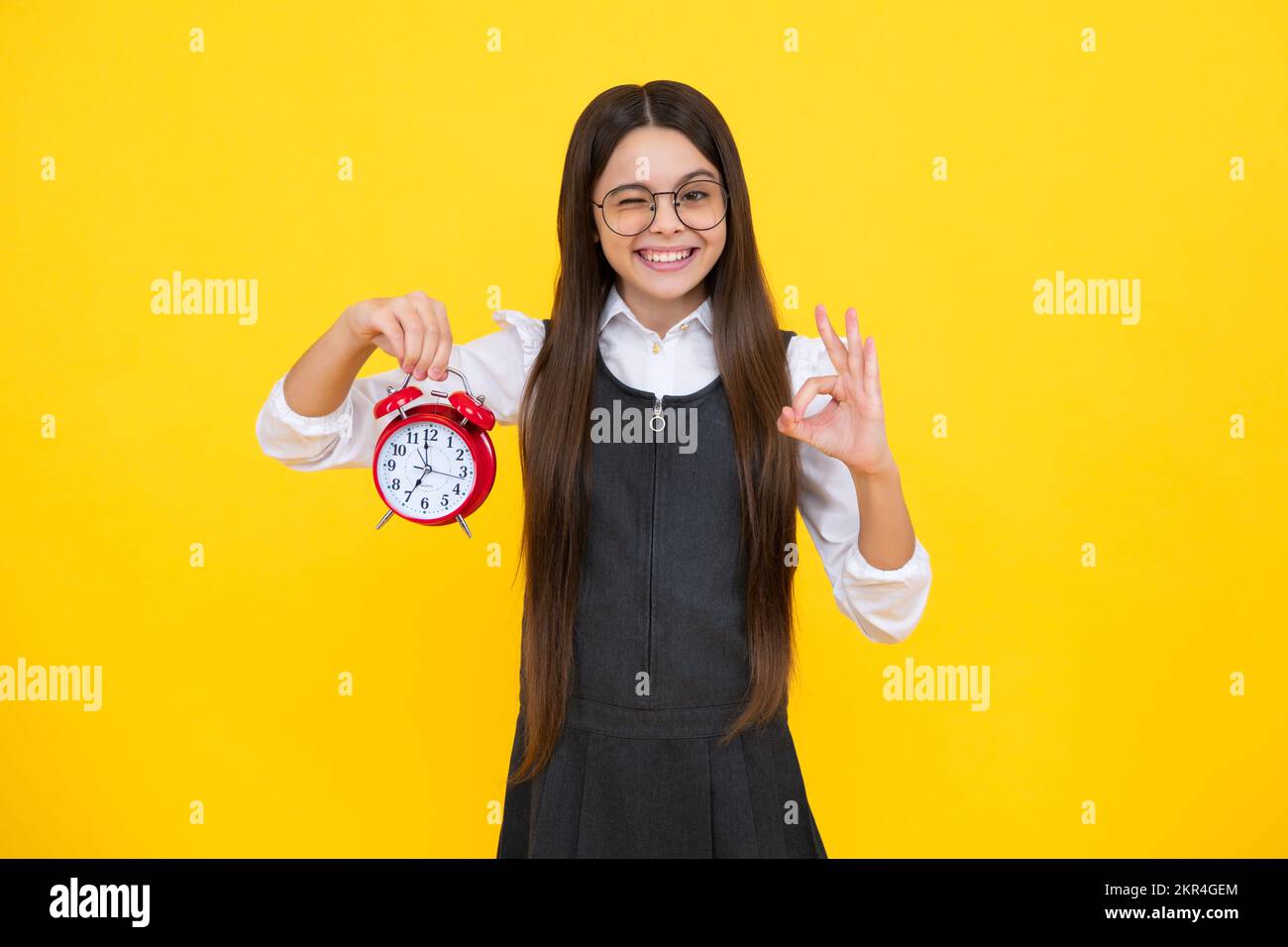 Funny face. Teen student girl hold clock isolated on yellow background ...