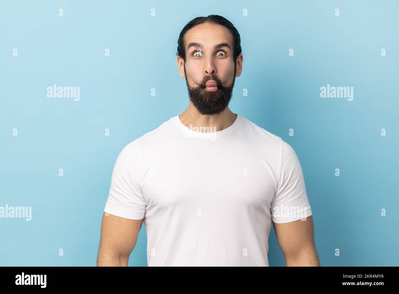 Portrait of childish man with beard wearing white T-shirt making fish ...
