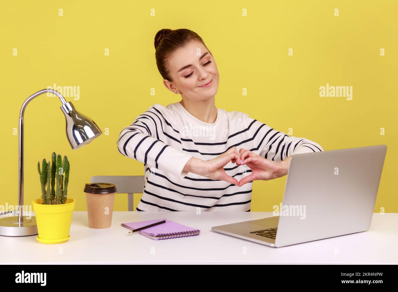 Positive woman showing heart gesture with hands to laptop screen ...