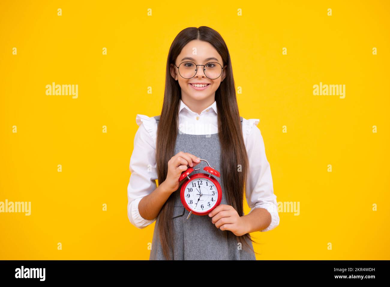 Teenager child hold clock isolated on yellow studio background ...