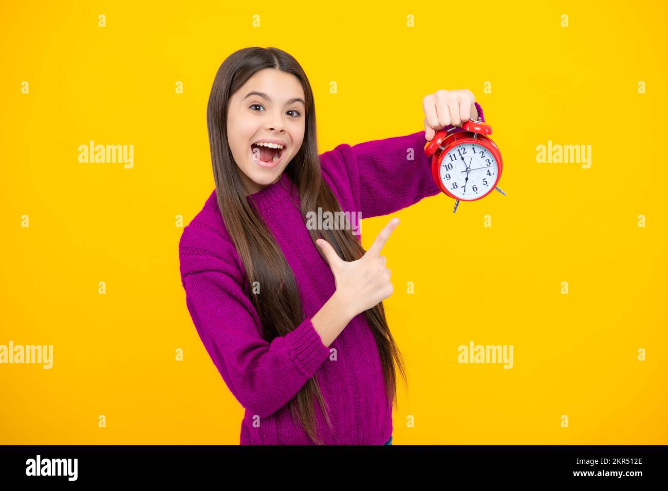 Excited face. Teen girl holding clock over yellow background. Early ...