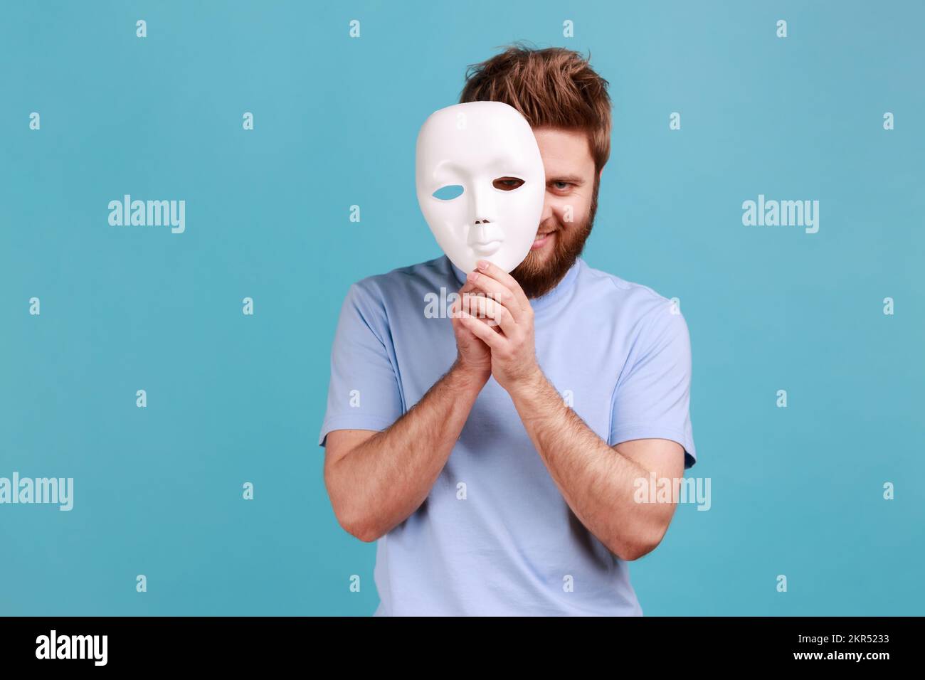 Portrait of positive bearded man removing white mask from face showing ...
