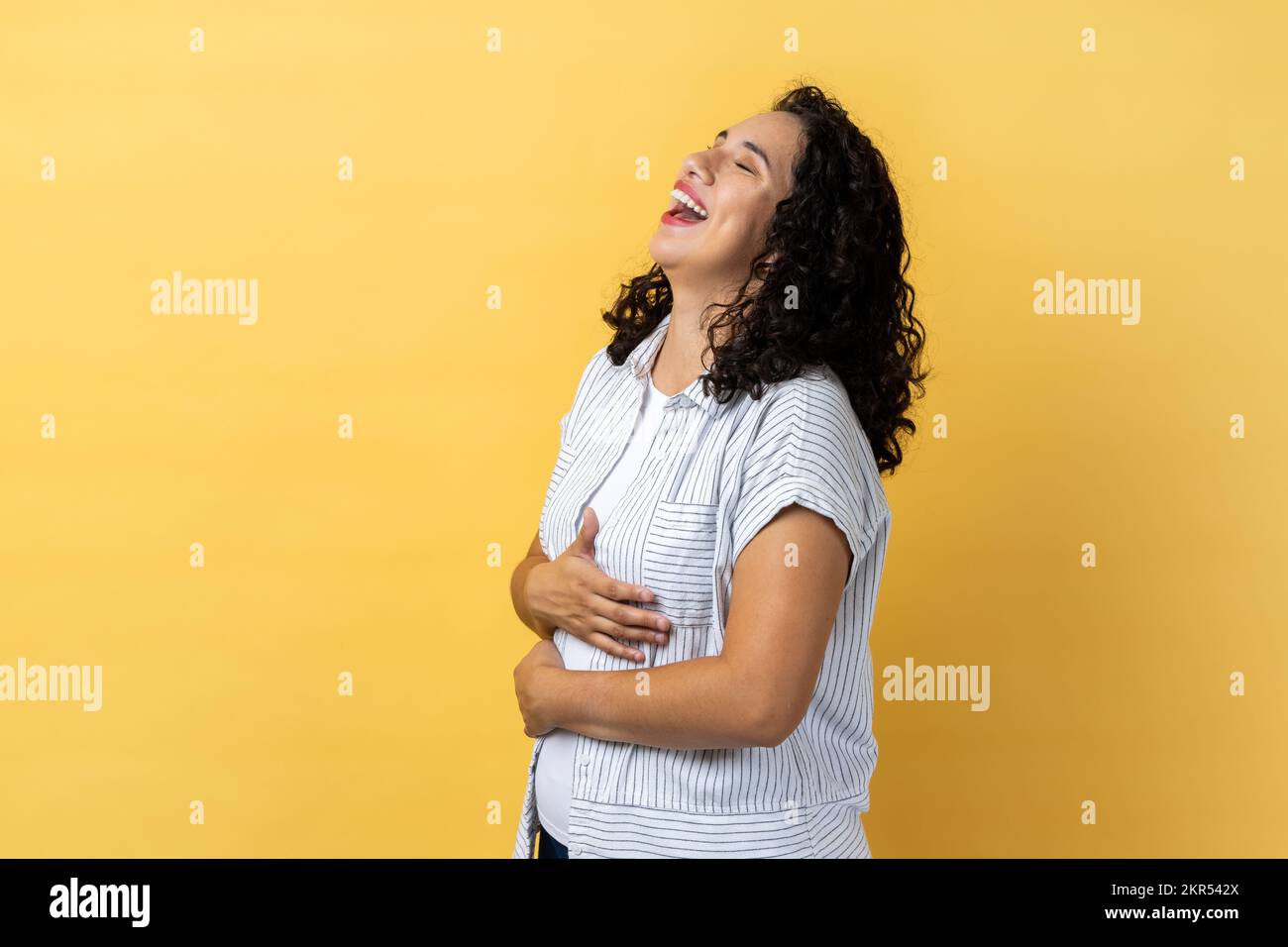 Portrait of overjoyed woman with dark wavy hair laughing happily at ...