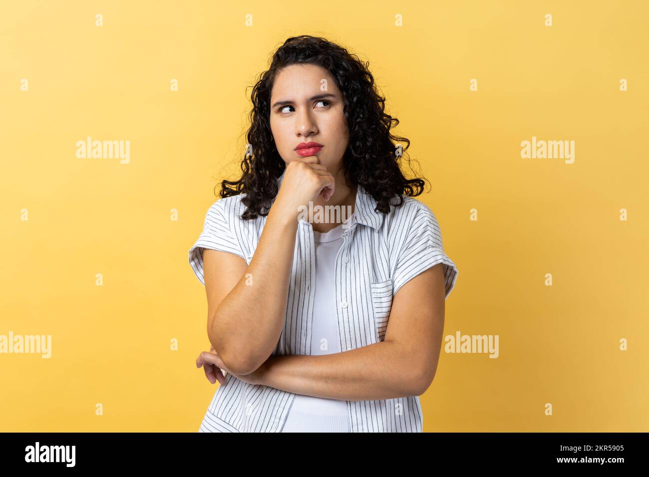 Hmm, I'm need thinking. Portrait of woman with dark wavy hair holding chin and musing, looking ...