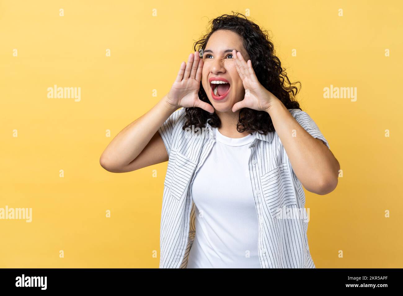 Portrait of attractive adorable woman with dark wavy hair opening mouth holding hands on face ...