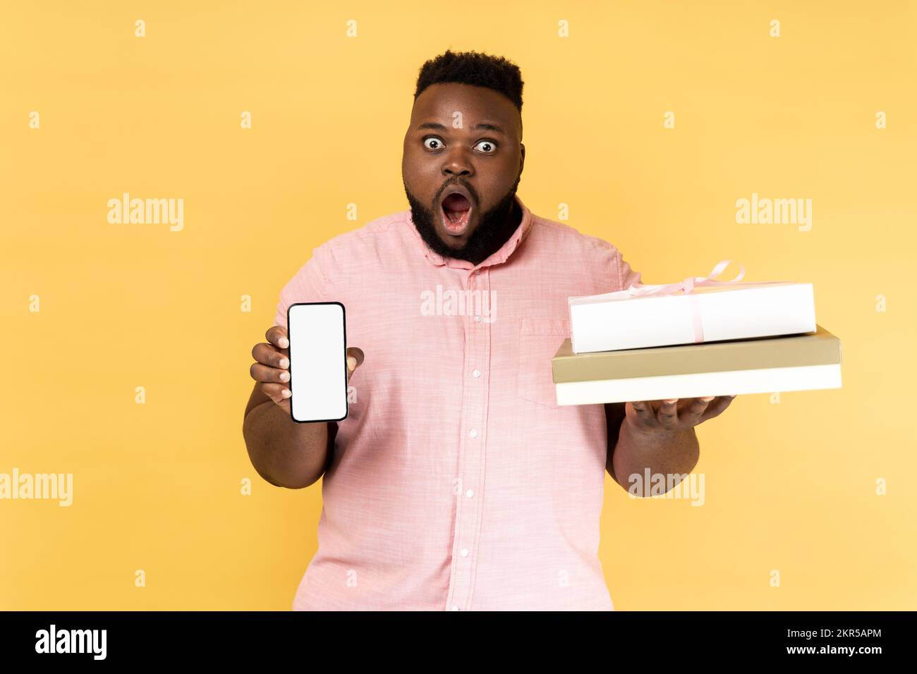 Portrait of shocked astonished man in pink shirt holding present box ...