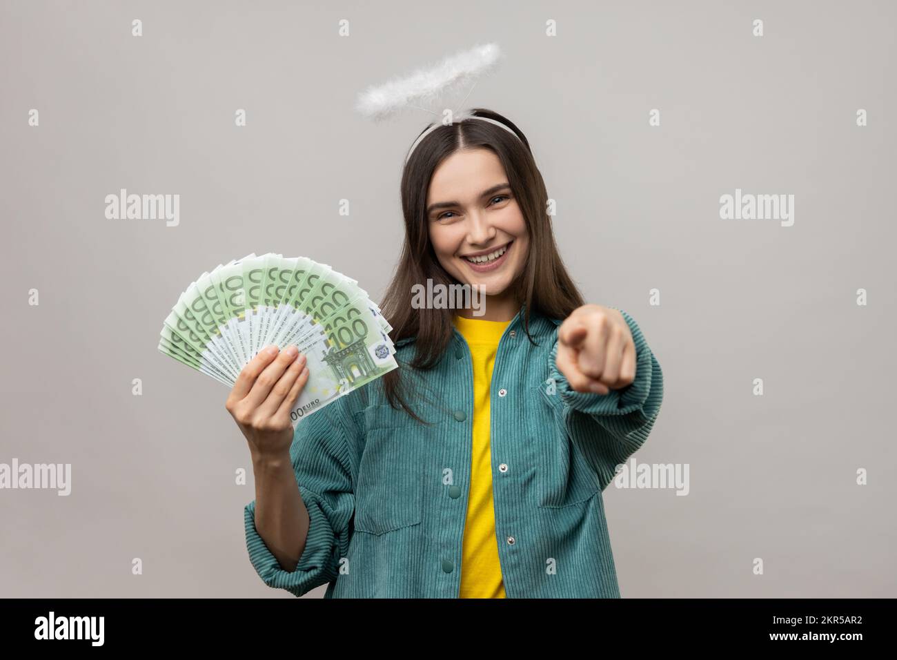 Positive angelic young woman with halo above head holding euro ...