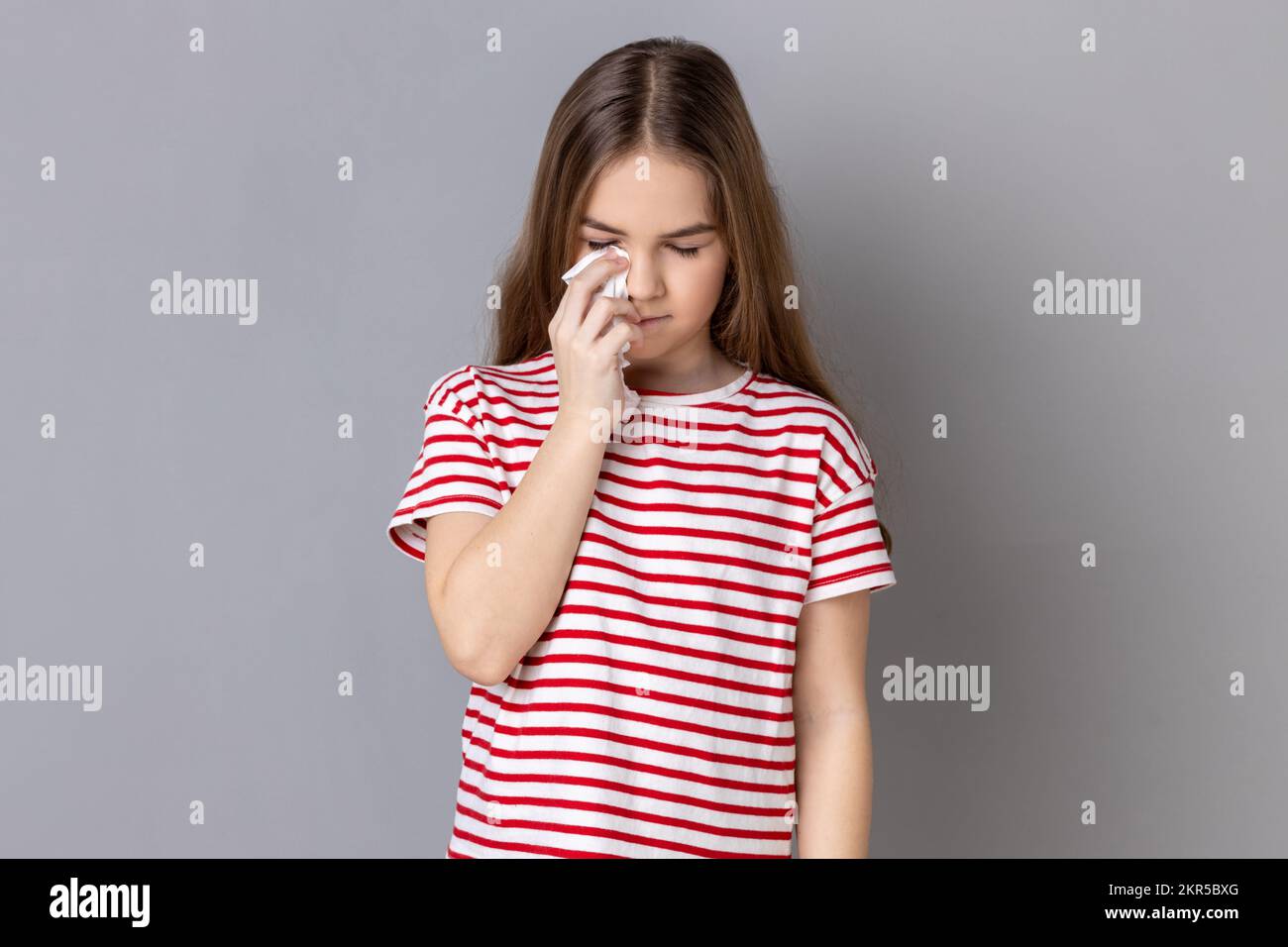 Portrait of unhappy sad little girl wearing striped T-shirt hiding face ...