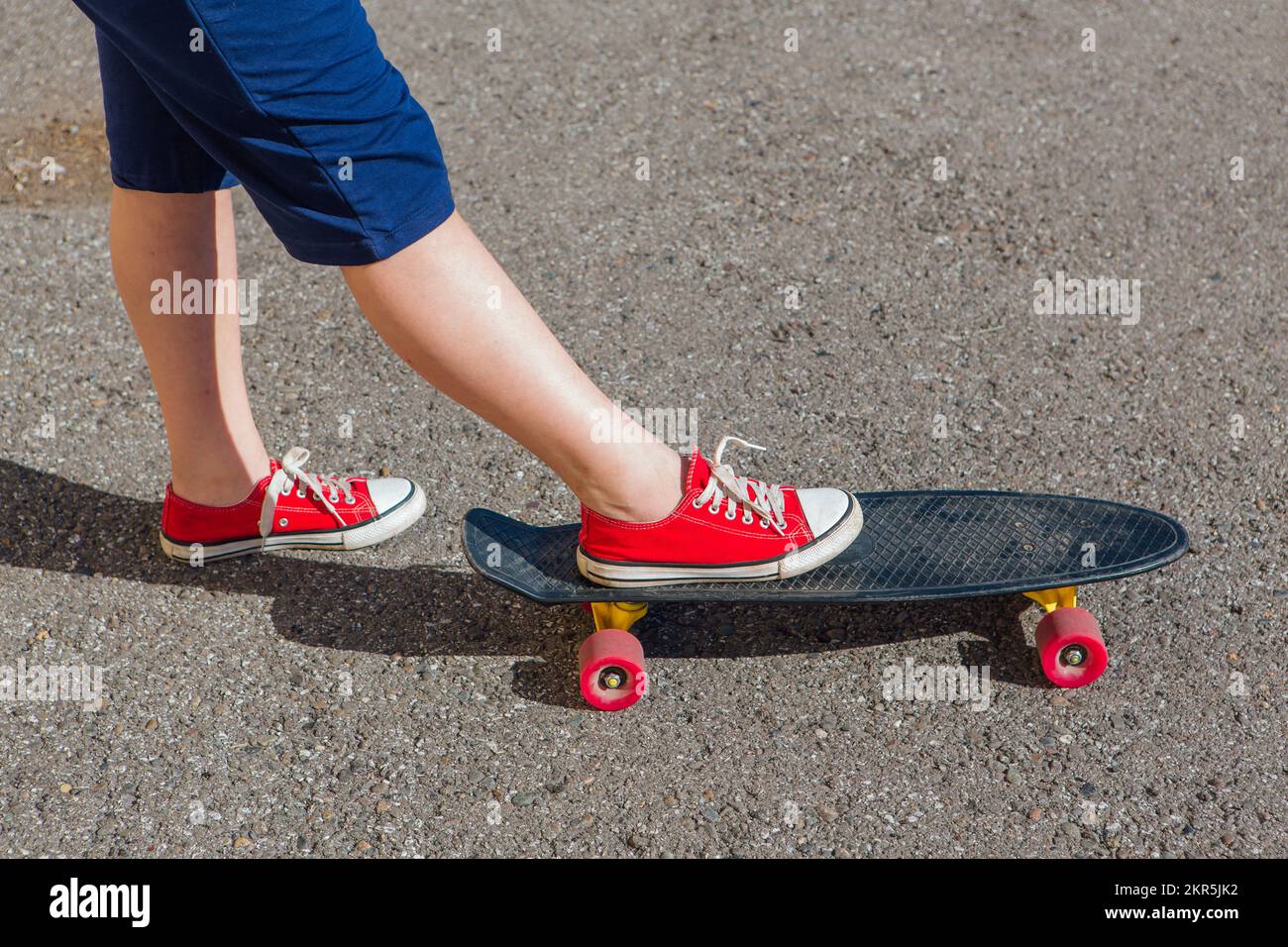 Close up of feet of a boy in red sneakers rides on black penny skate ...