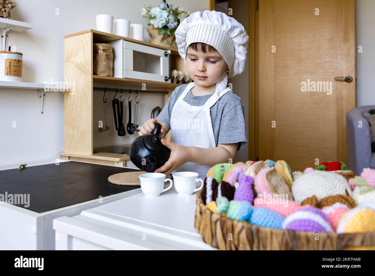 Cute little baby boy in chef hat and apron playing at childish kitchen ...