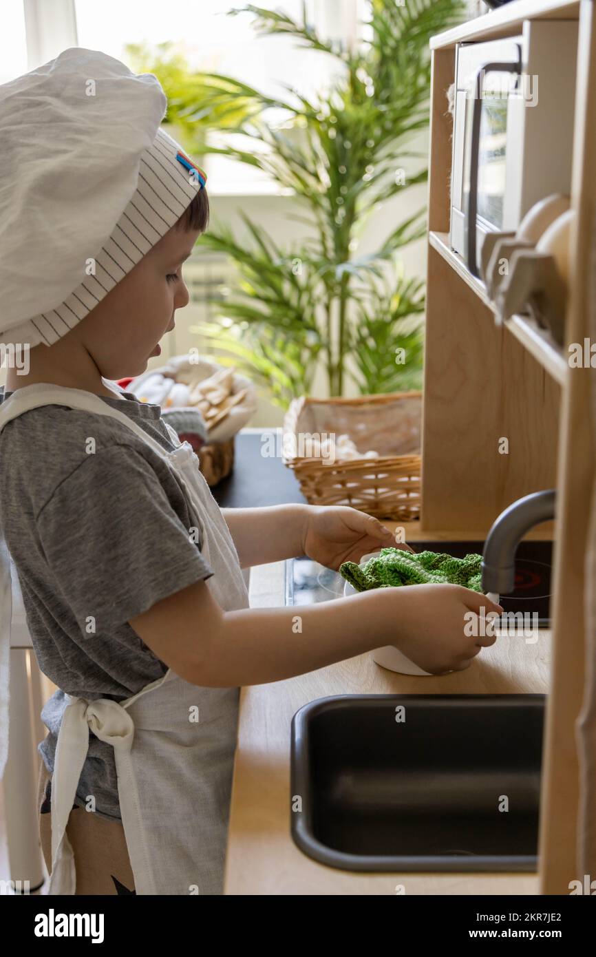 Cute little baby boy in chef hat and apron playing at childish kitchen ...