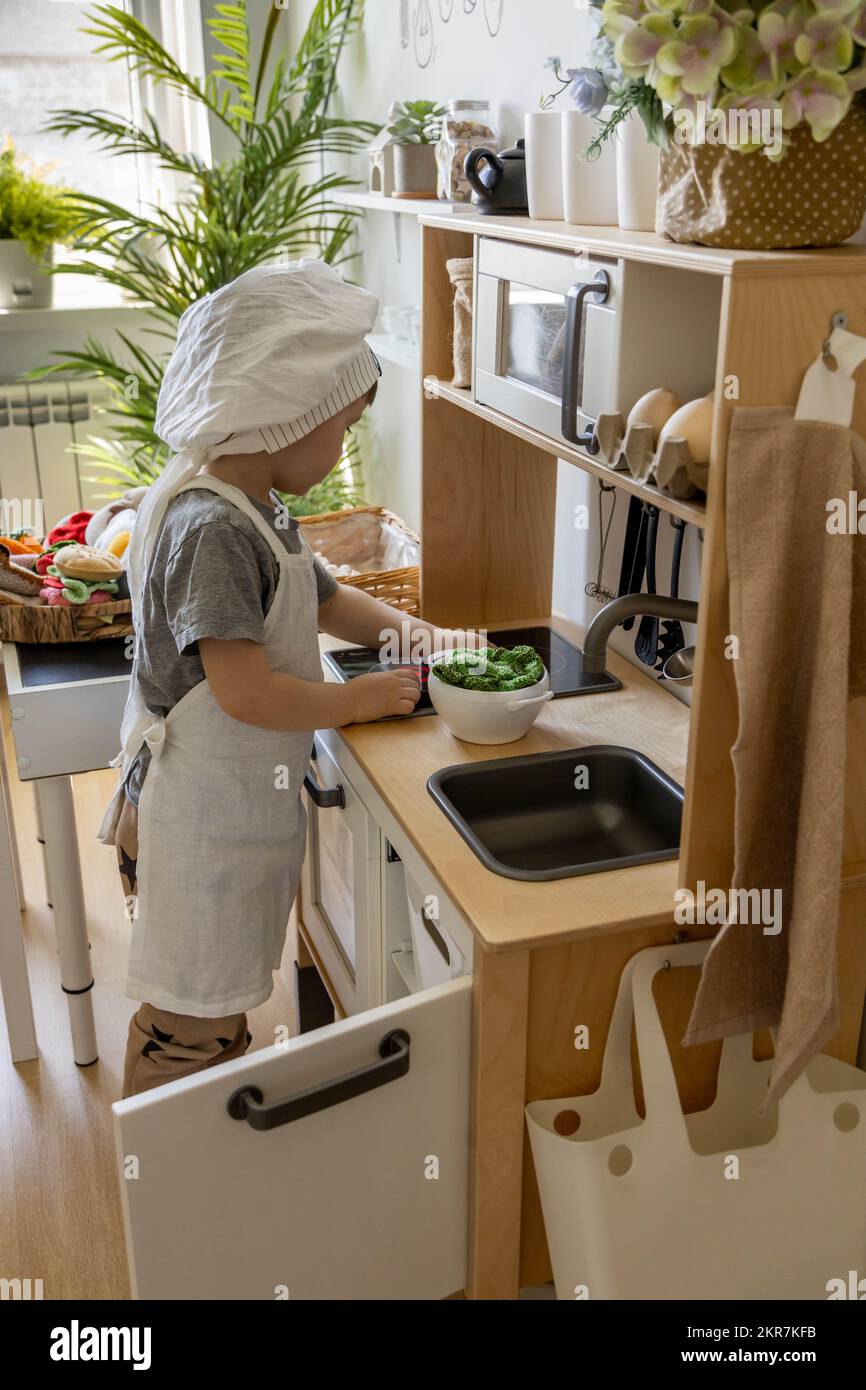 Cute little baby boy in chef hat and apron playing at childish kitchen ...