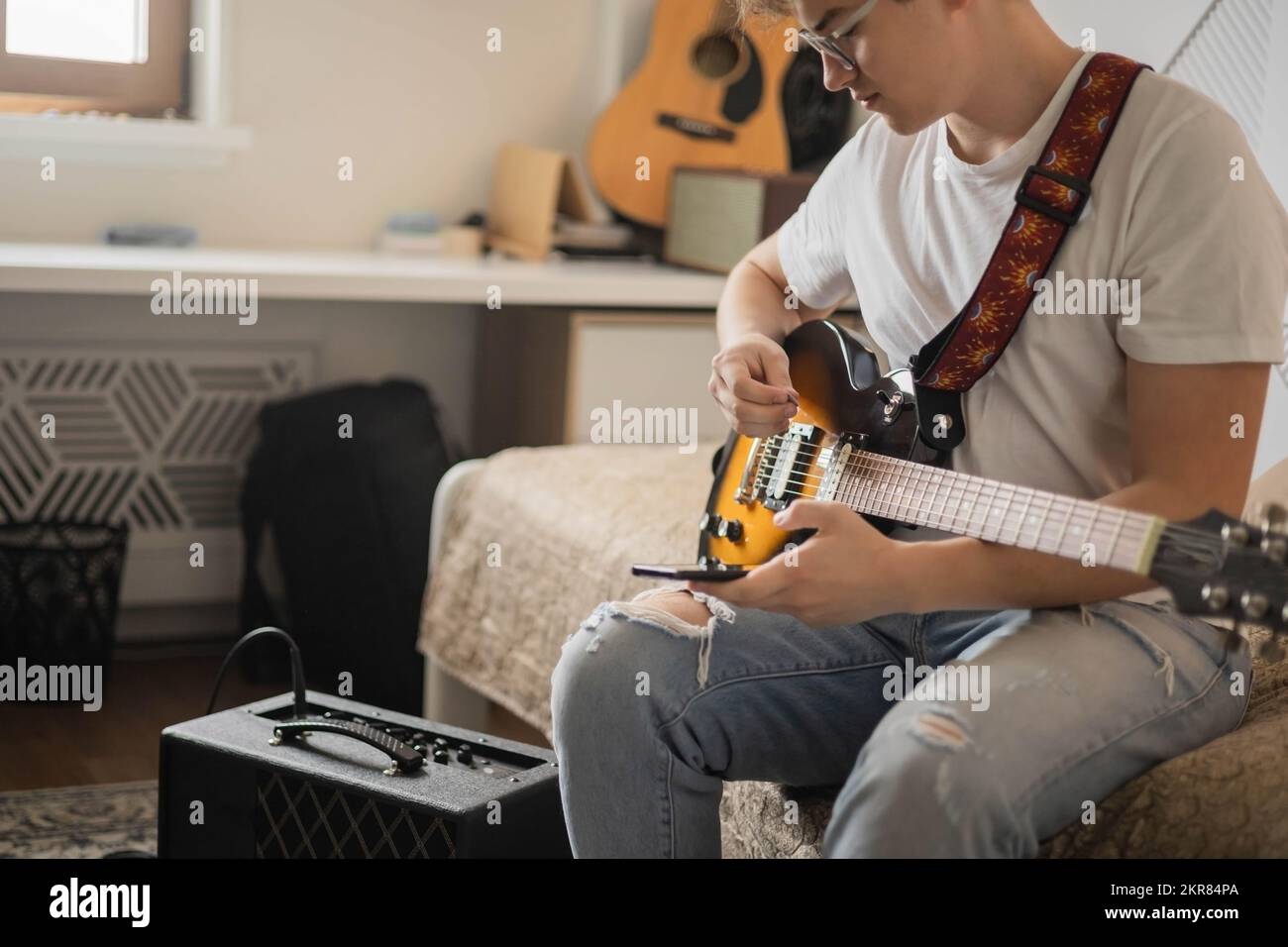 Young man playing electric guitar singing song sitting on bed at home ...