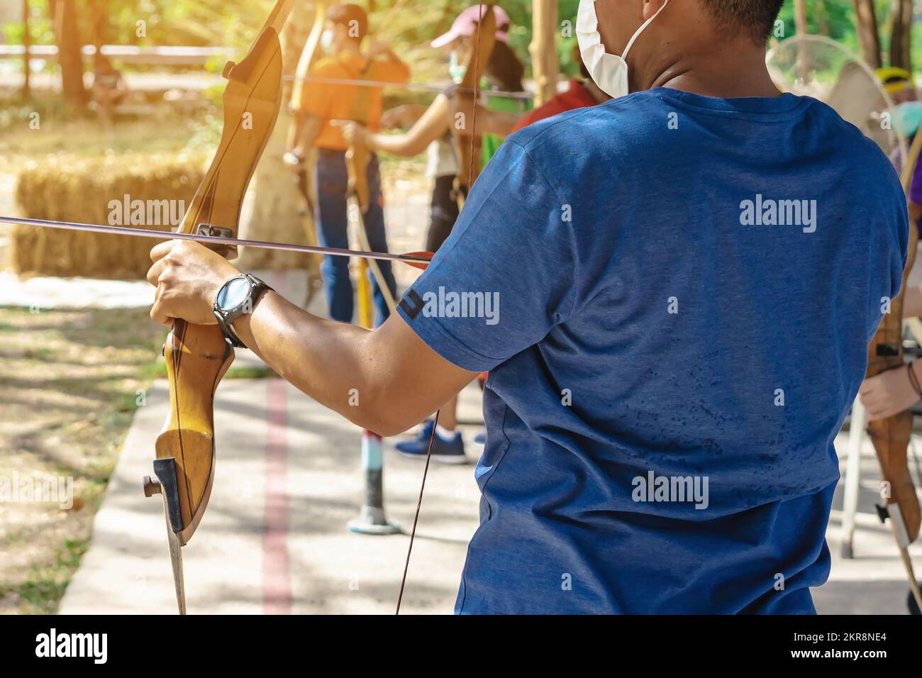 Back view of young man aims archery bow and arrow to colorful target in ...