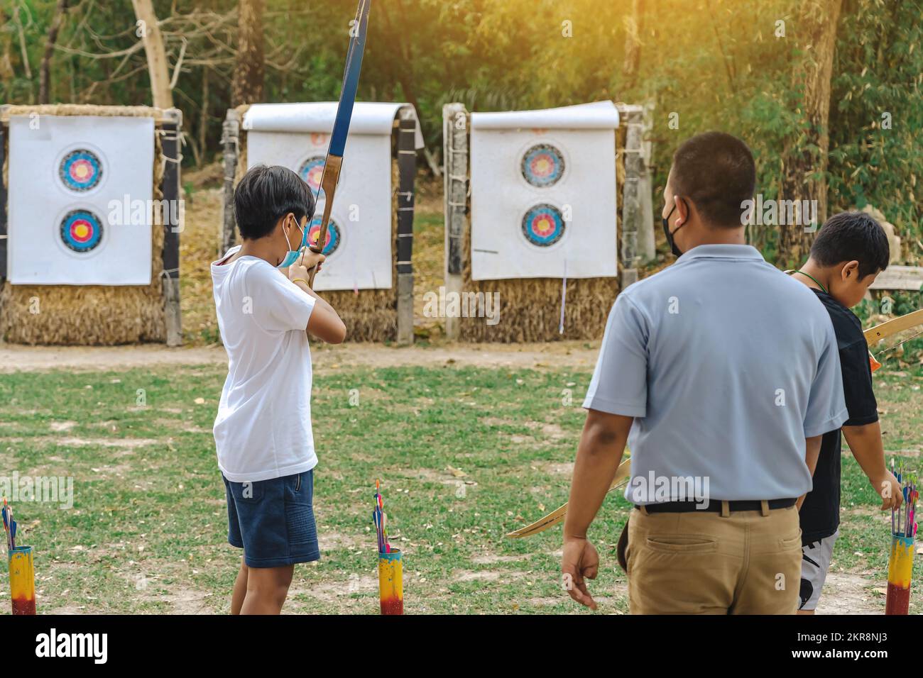Back view of Asian boy wear face mask aims archery bow and arrow to ...