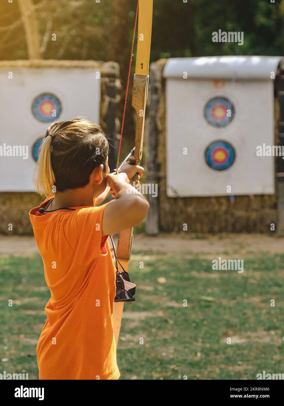 Back view of Asian boy wear face mask aims archery bow and arrow to ...