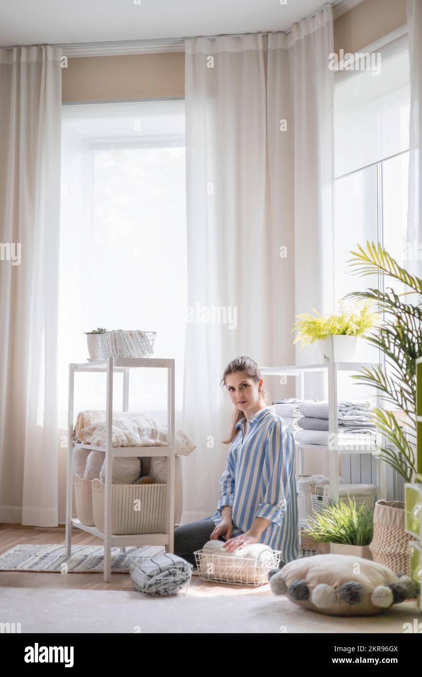 Domestic woman in pajamas neatly putting folded linens into cupboard ...