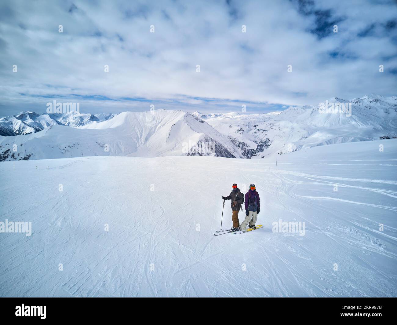 Skier and snowboarder standing on mountain top against blue sky and ...