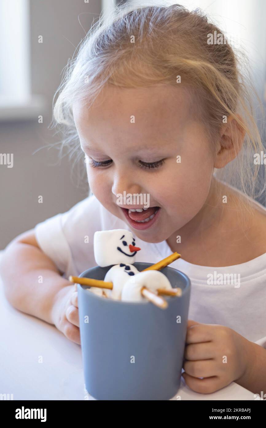 Little cute children eats a marmmello snowman decorated with icing and ...