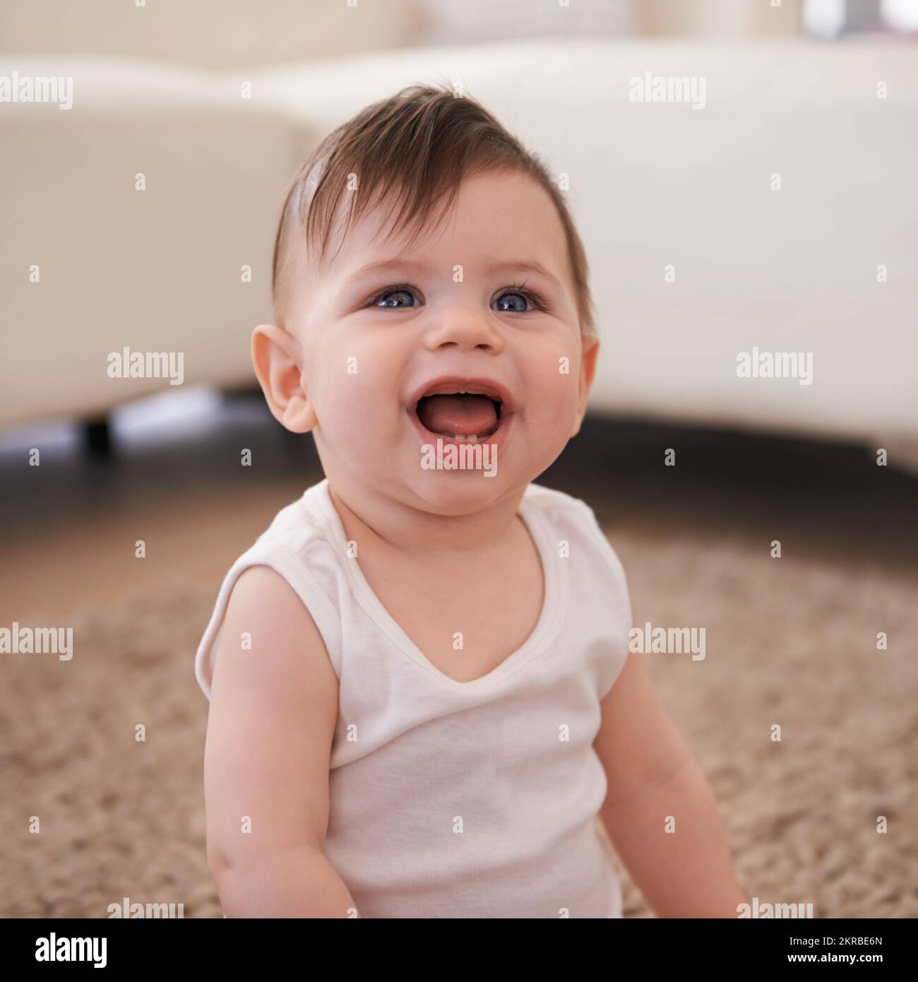 Delightfully adorable. a baby boy sitting on the carpet at home Stock ...
