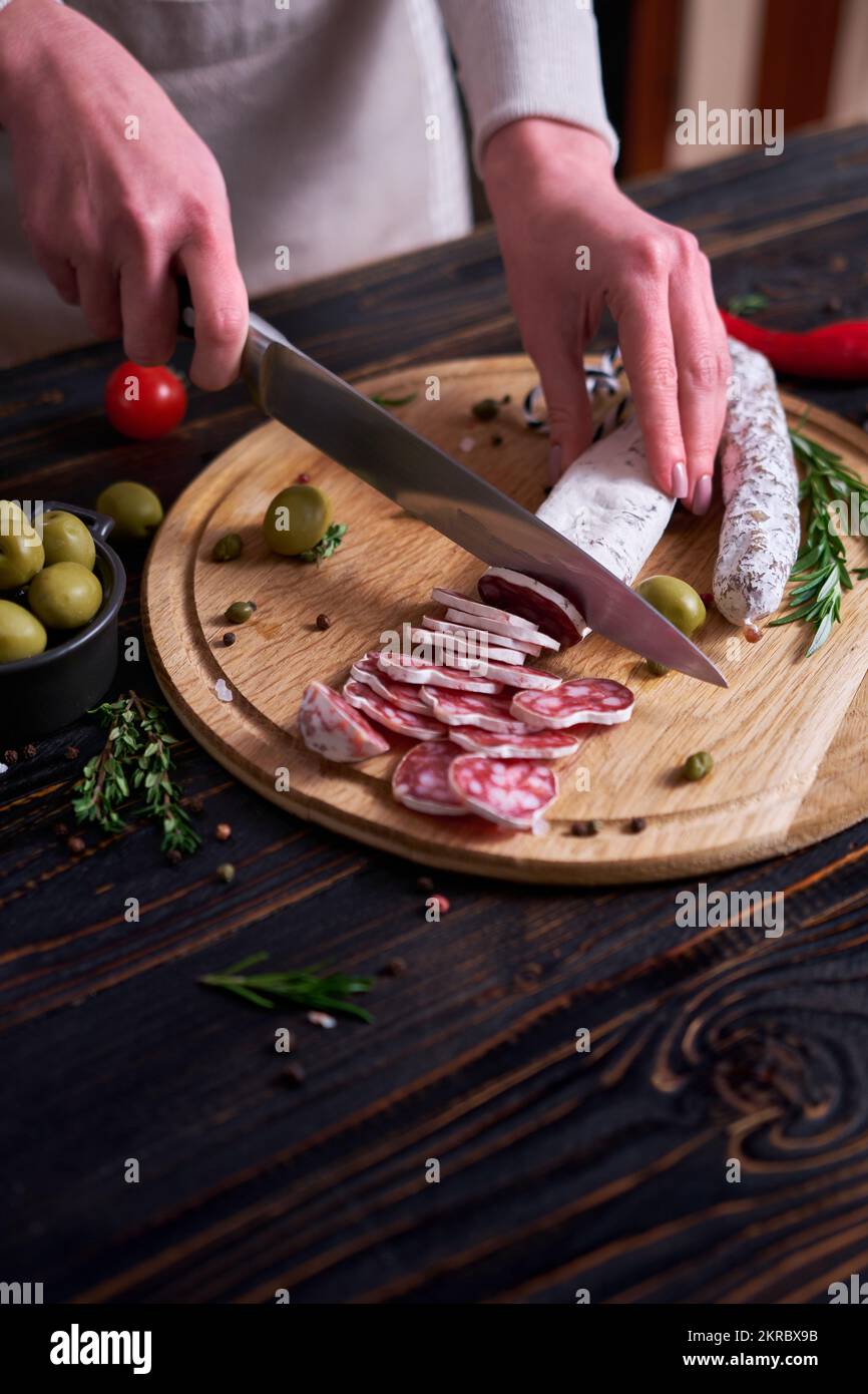 Woman slicing Spanish fuet salami sausageon wooden cutting board at ...