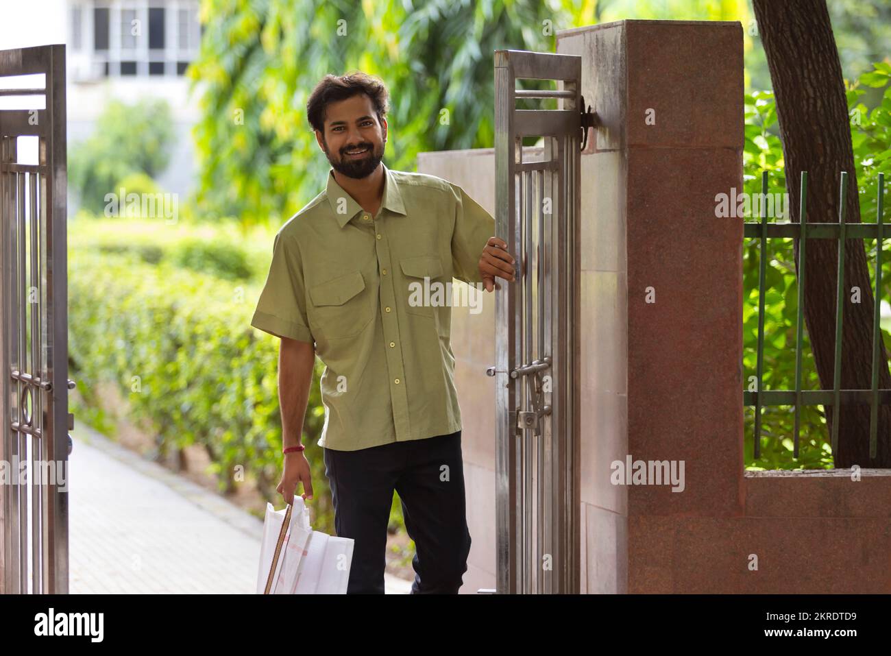 Young man standing at entrance gate with a shopping bag Stock Photo - Alamy