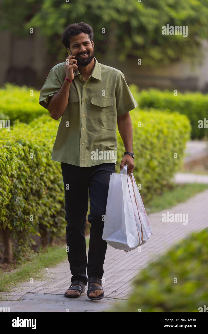 Young man talking on mobile phone while walking through park Stock ...
