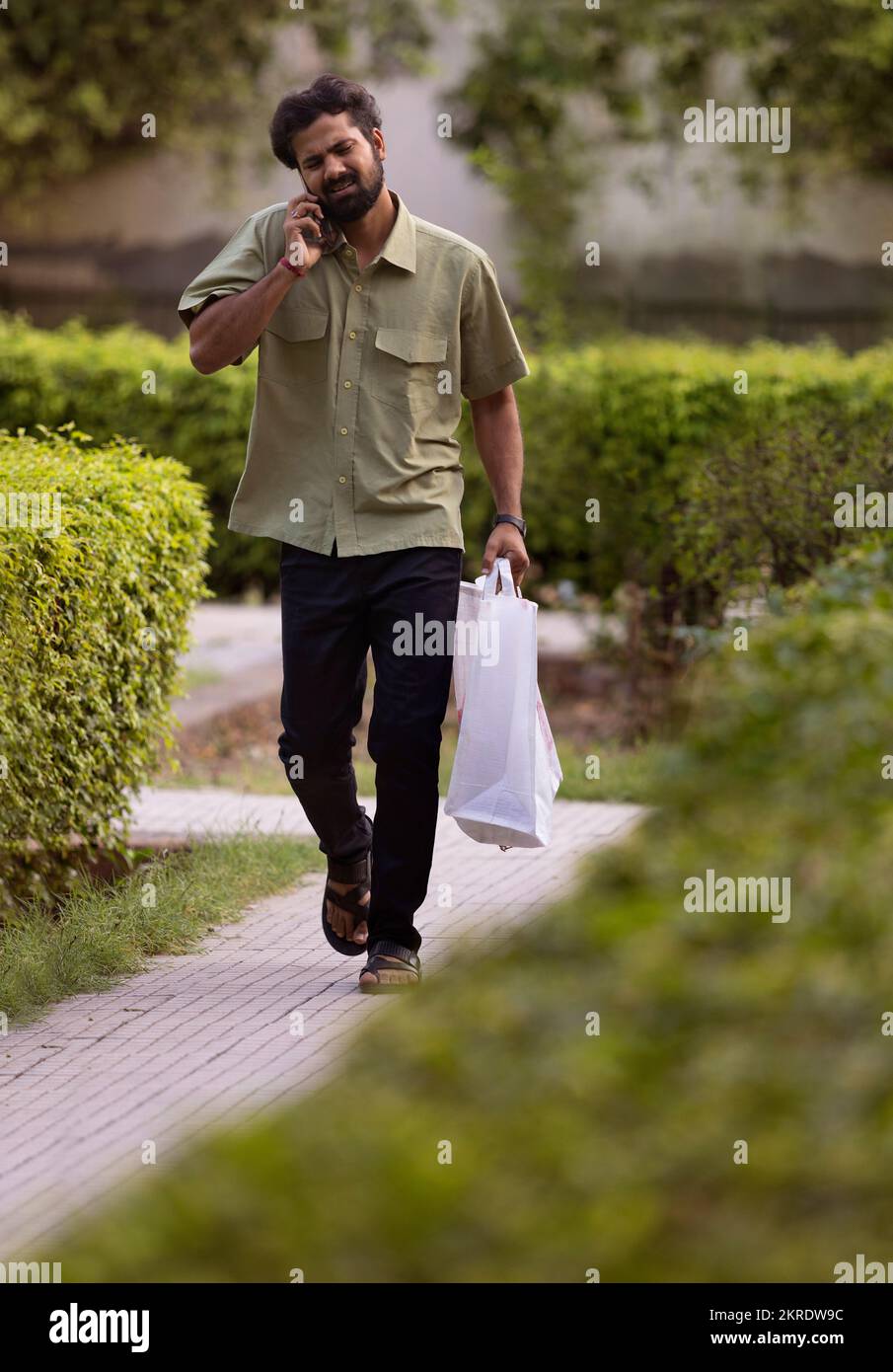 Young man talking on mobile phone while walking through park Stock ...