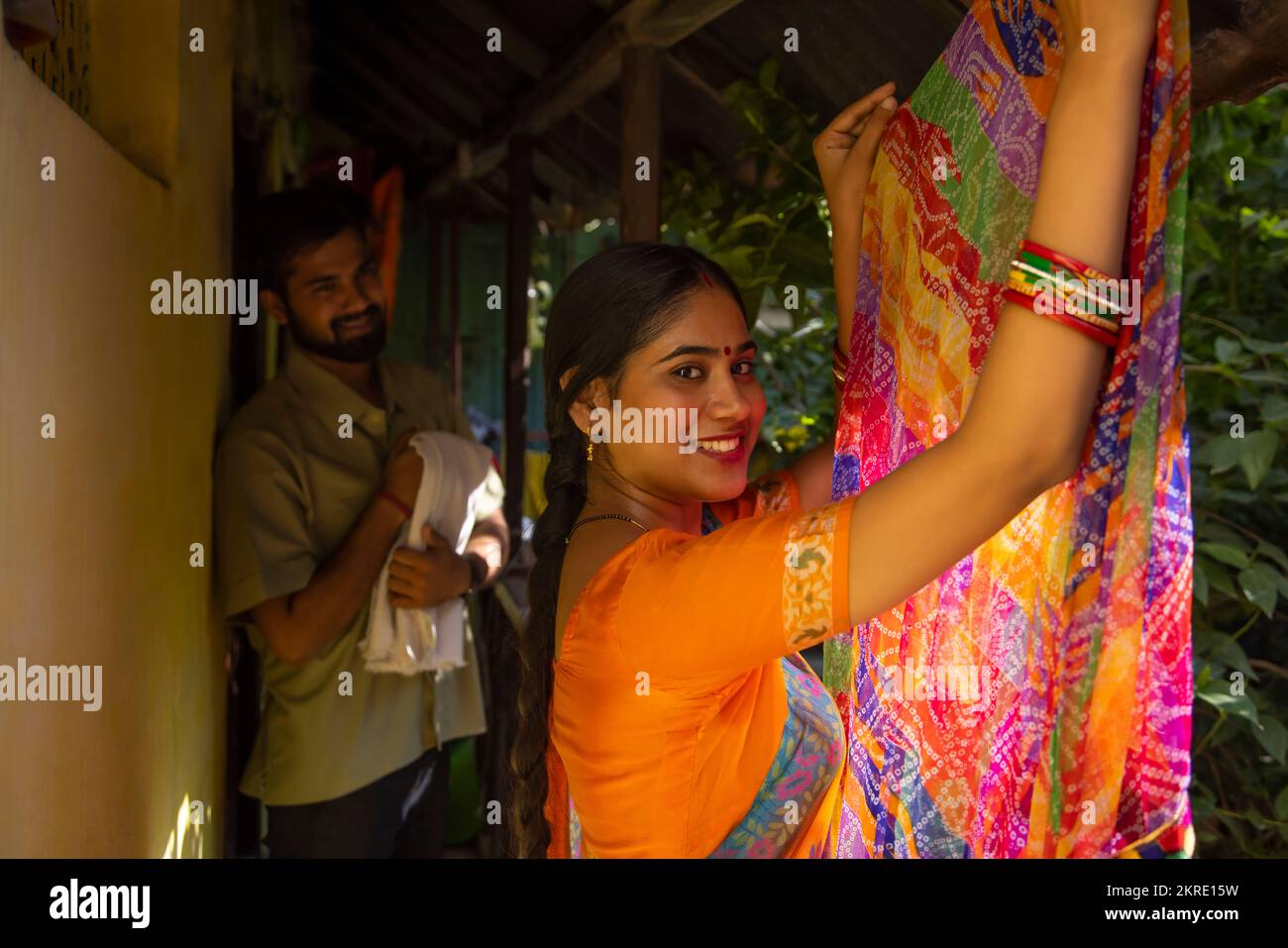 Smiling woman hanging cloth on laundry line and husband standing behind ...