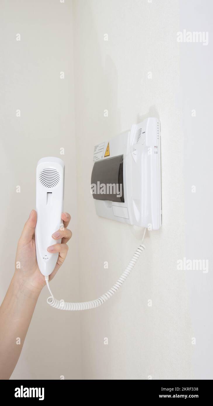 Intercom handset in a man's hand against the background of a white wall ...