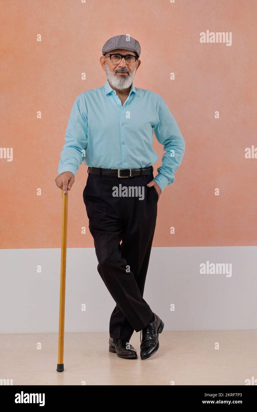 Portrait of senior man in formal outfit standing with walking stick ...