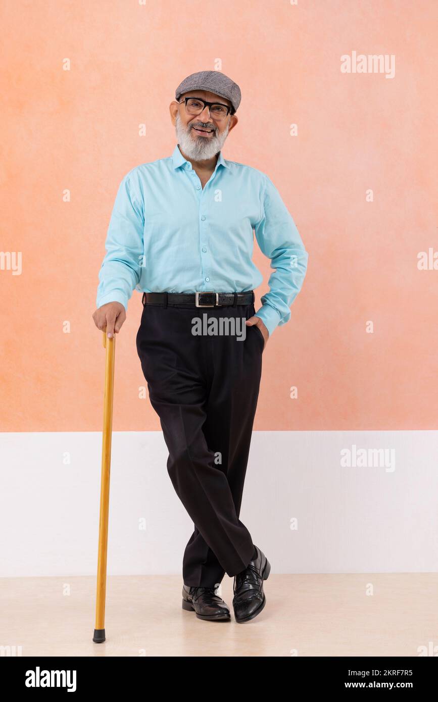 Portrait of senior man in formal outfit standing with walking stick ...
