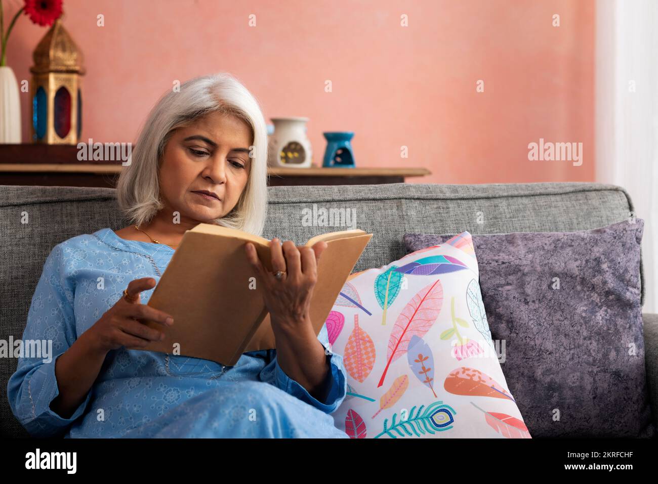 Old woman reading a book while sitting on sofa at home Stock Photo - Alamy