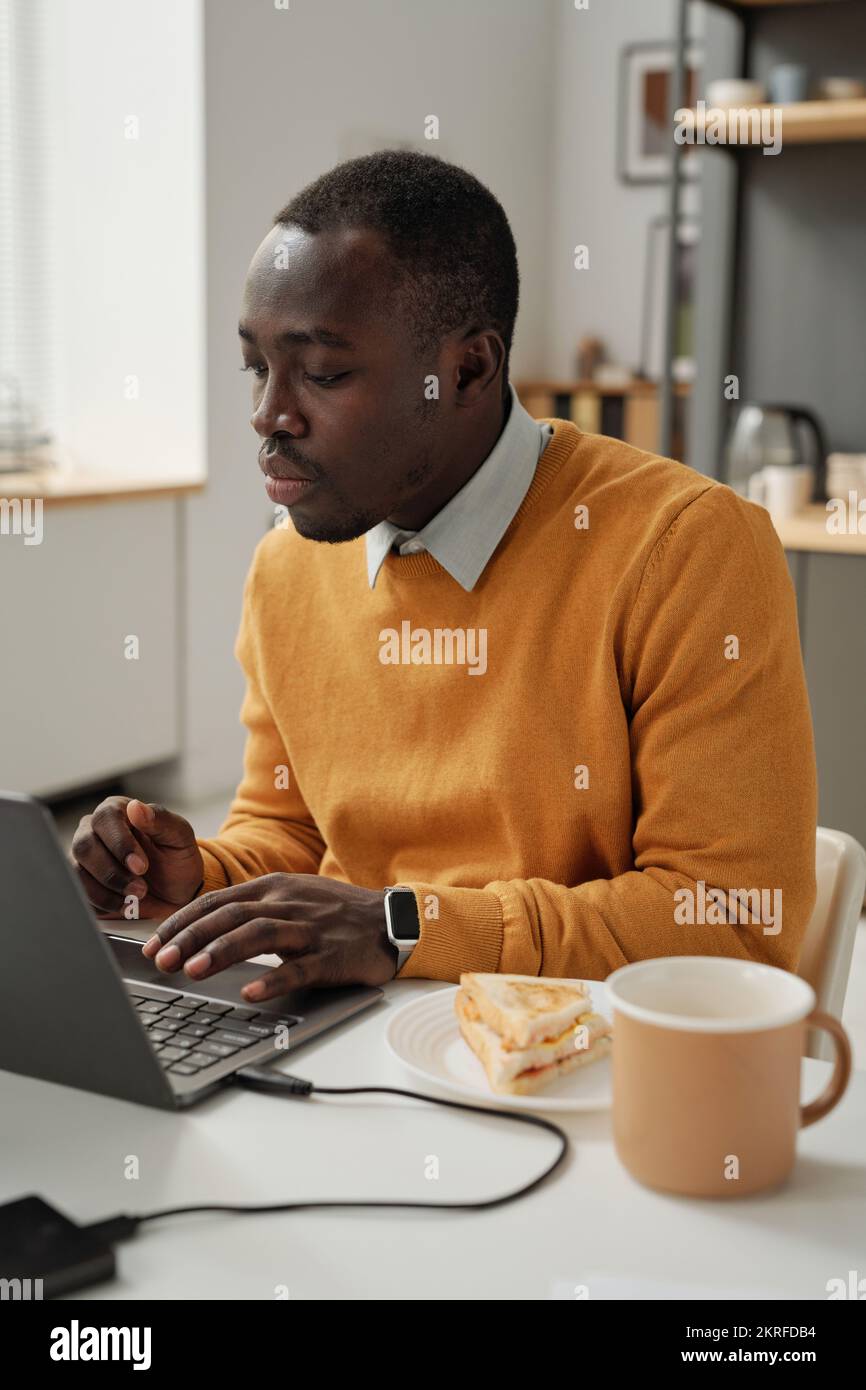 African American programmer working on laptop and eating sandwich with ...