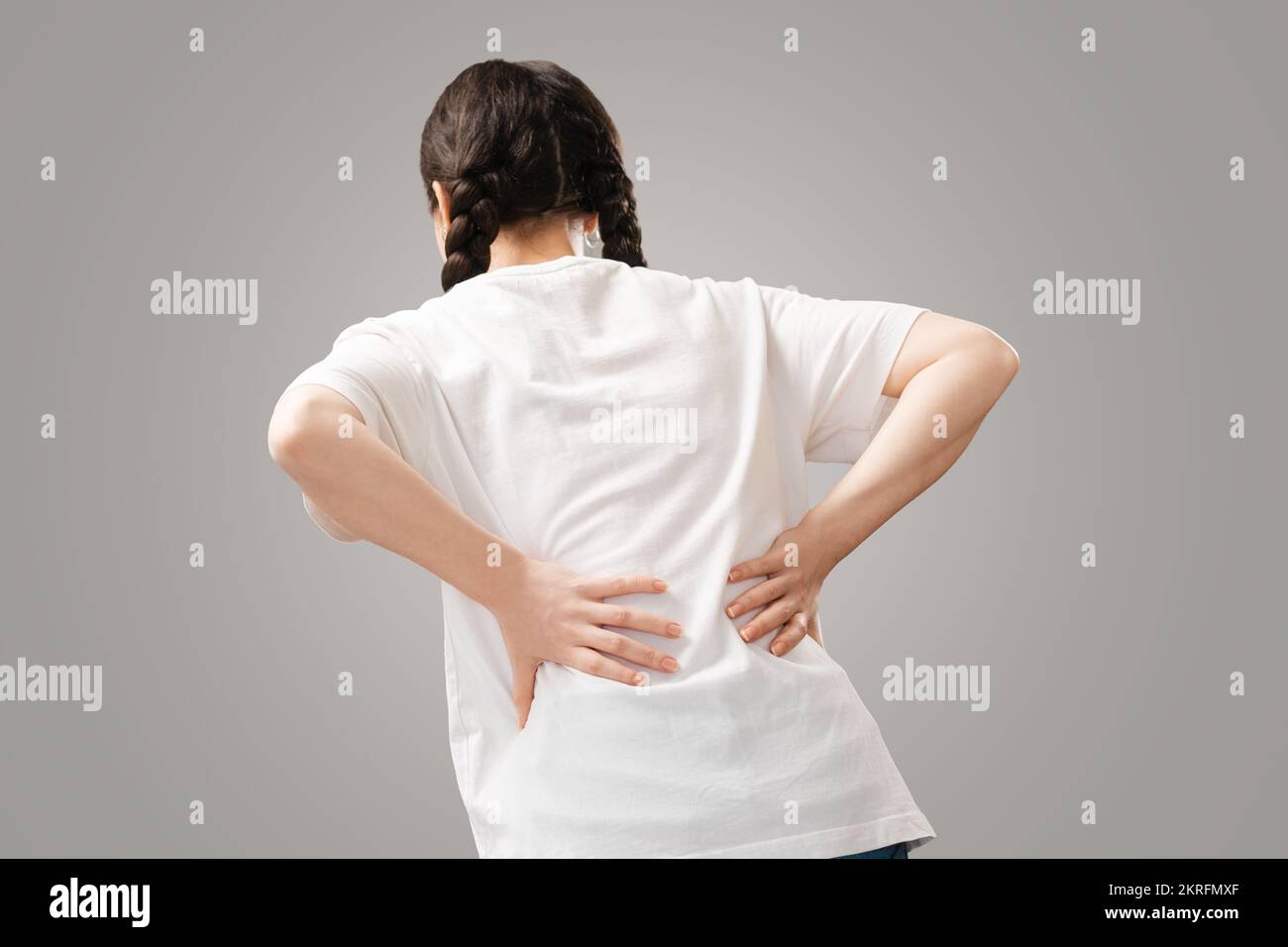 Back pain. The woman holds her hands to the small of her back. Rear ...