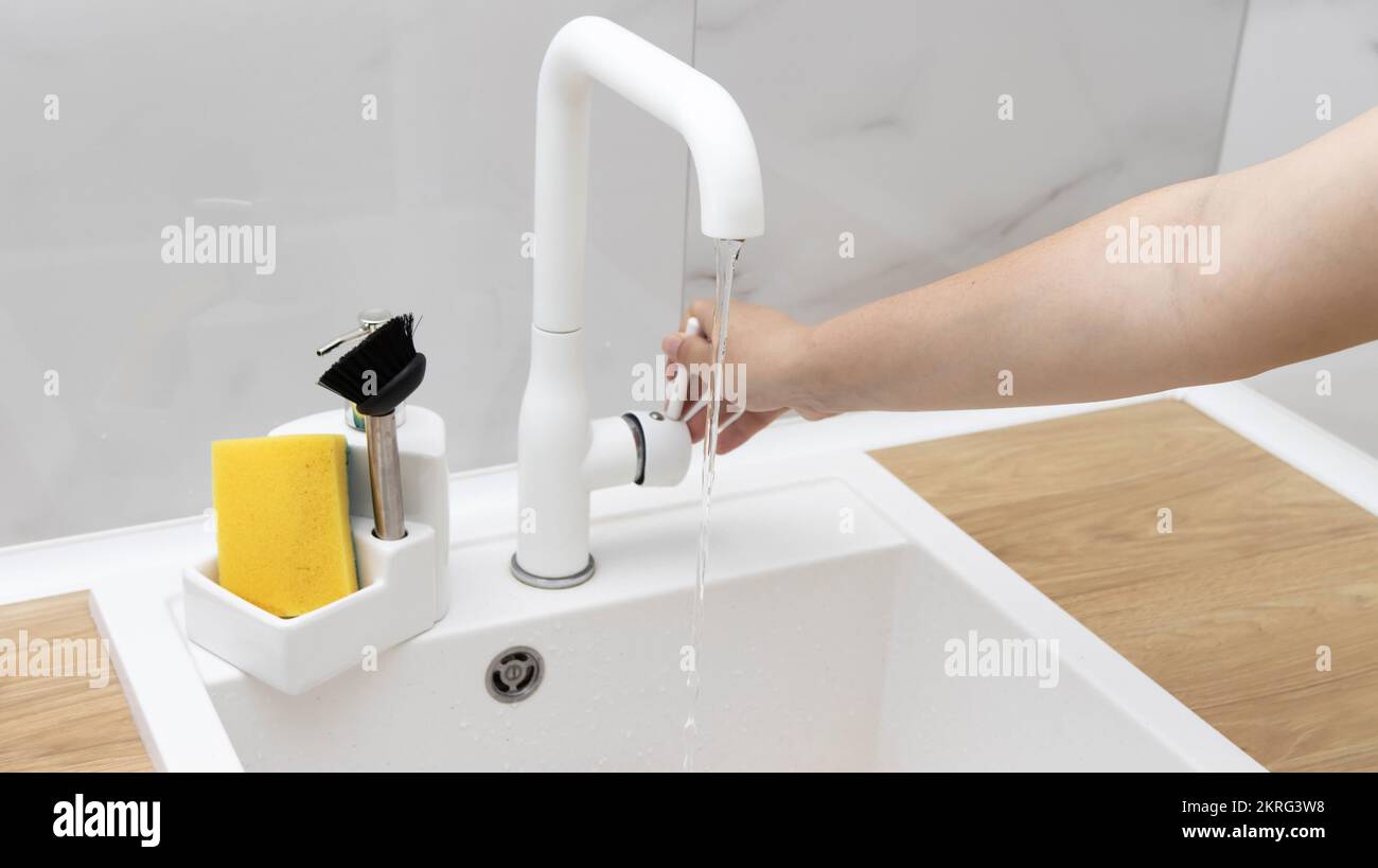 The girl opens a modern white water faucet in the kitchen. Detergent ...