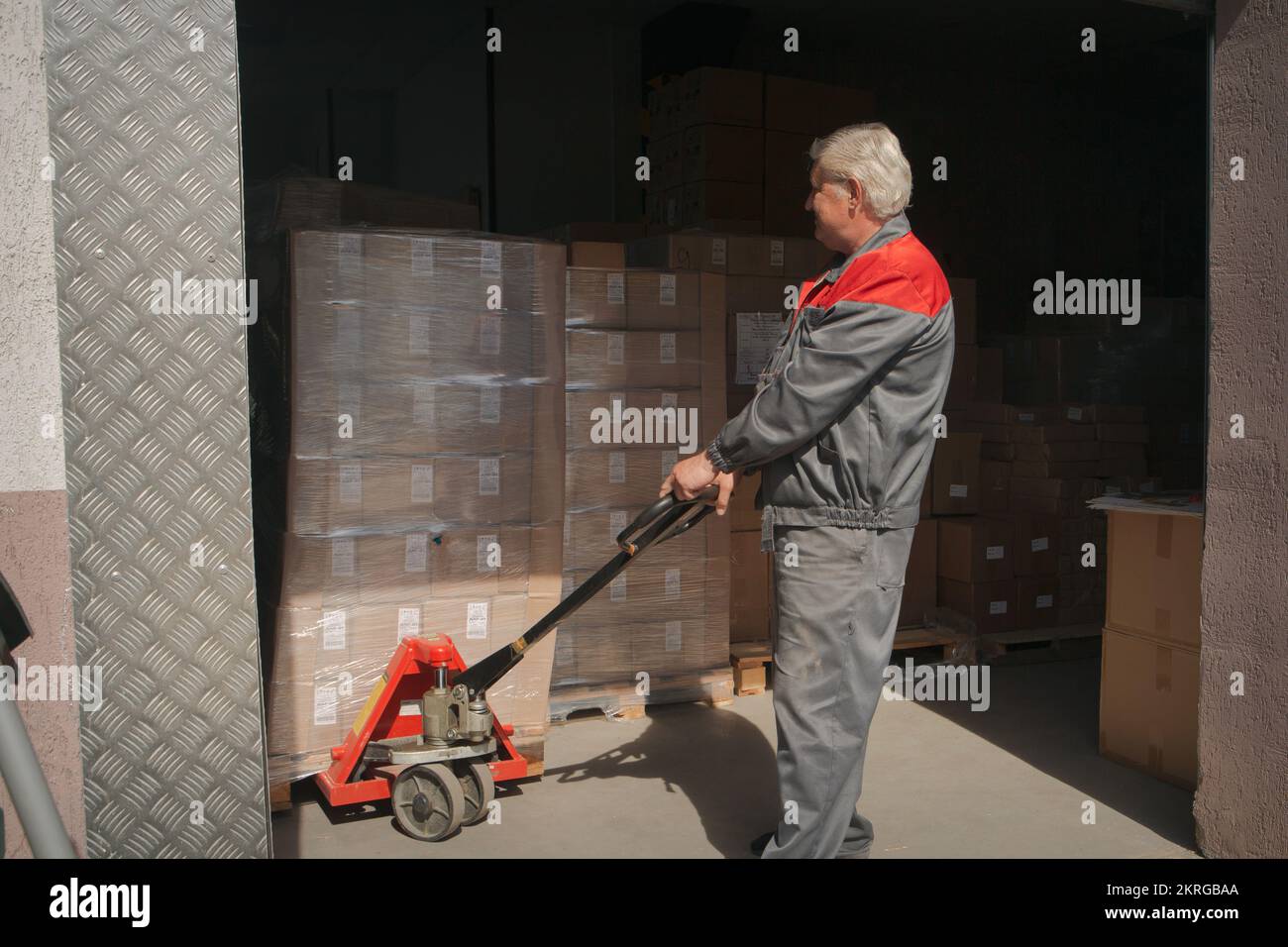 A loader rolls a trolley in a warehouse among many boxes. High quality ...