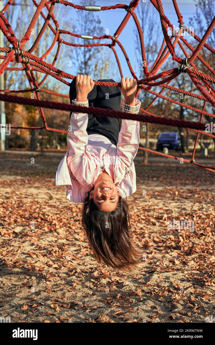 Full body of happy teen girl hanging upside down on red rope web in ...