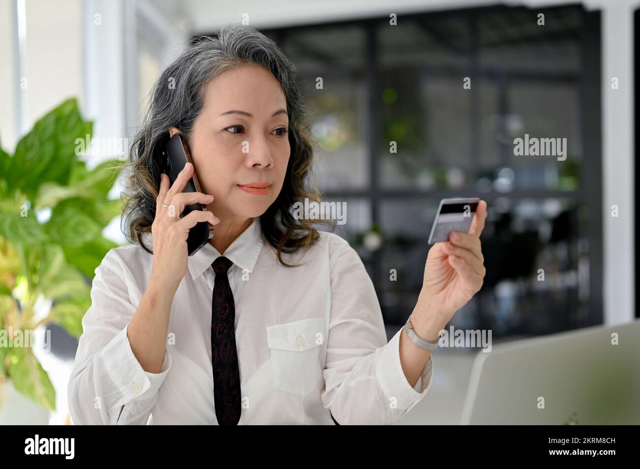 Attractive Asian aged businesswoman holding a credit card, calling to ...