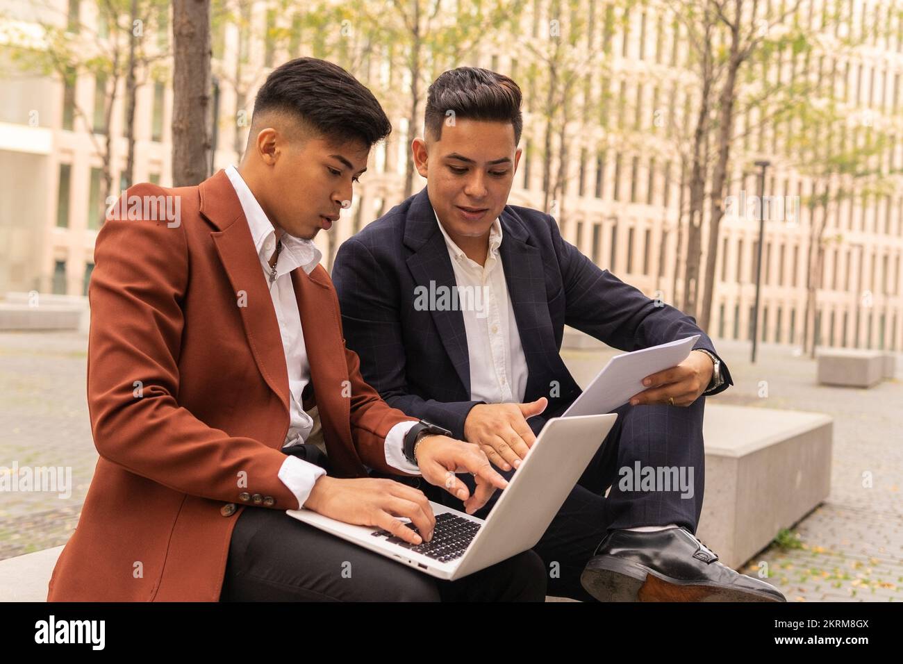 Focused Hispanic businessmen in classy outfits with documentation using laptop while working ...