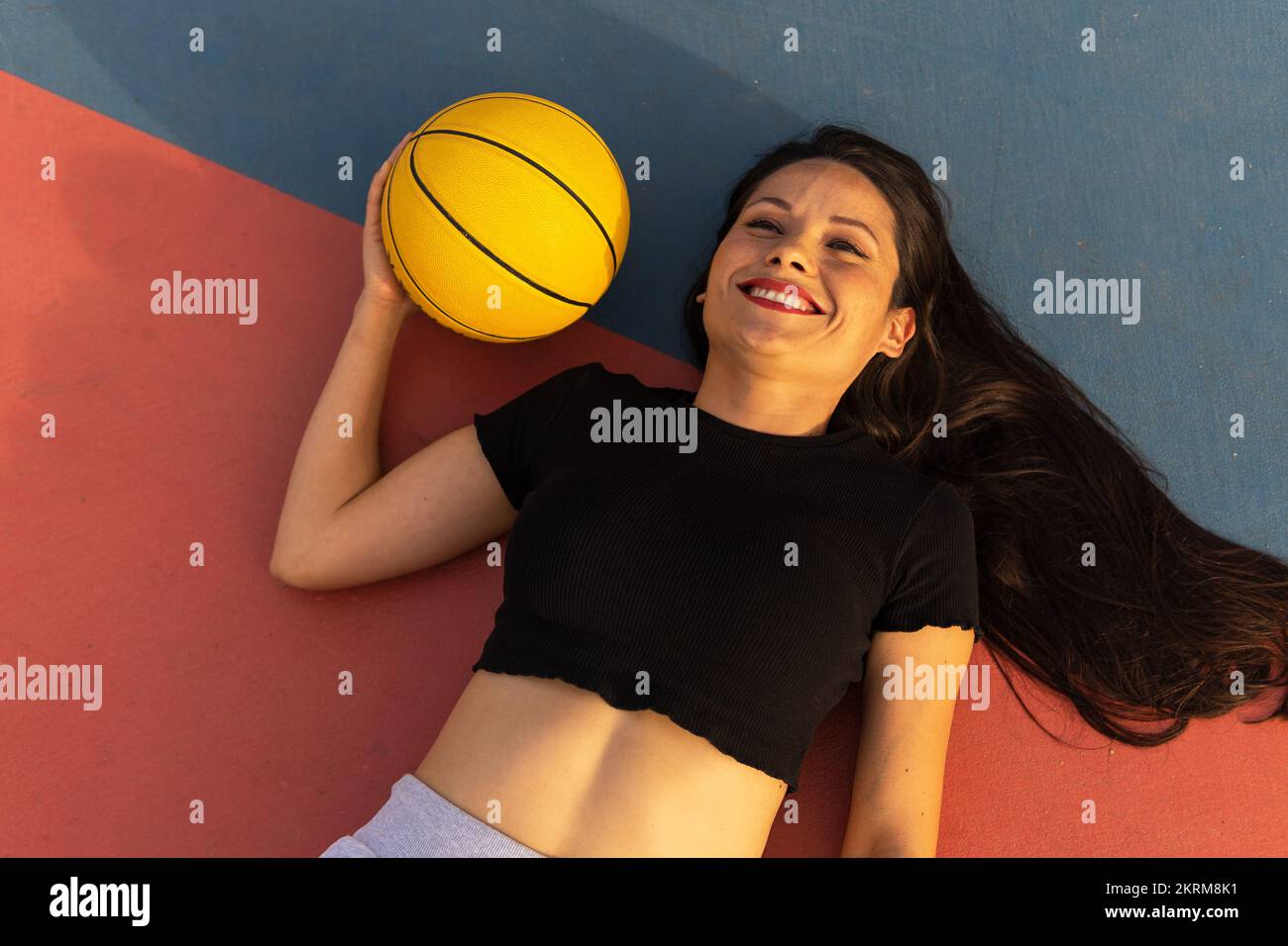 Top view of smiling female in crop top lying on ground on court with ...