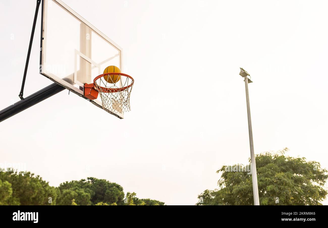 Low angle of orange ball falling into basketball ring with net during ...