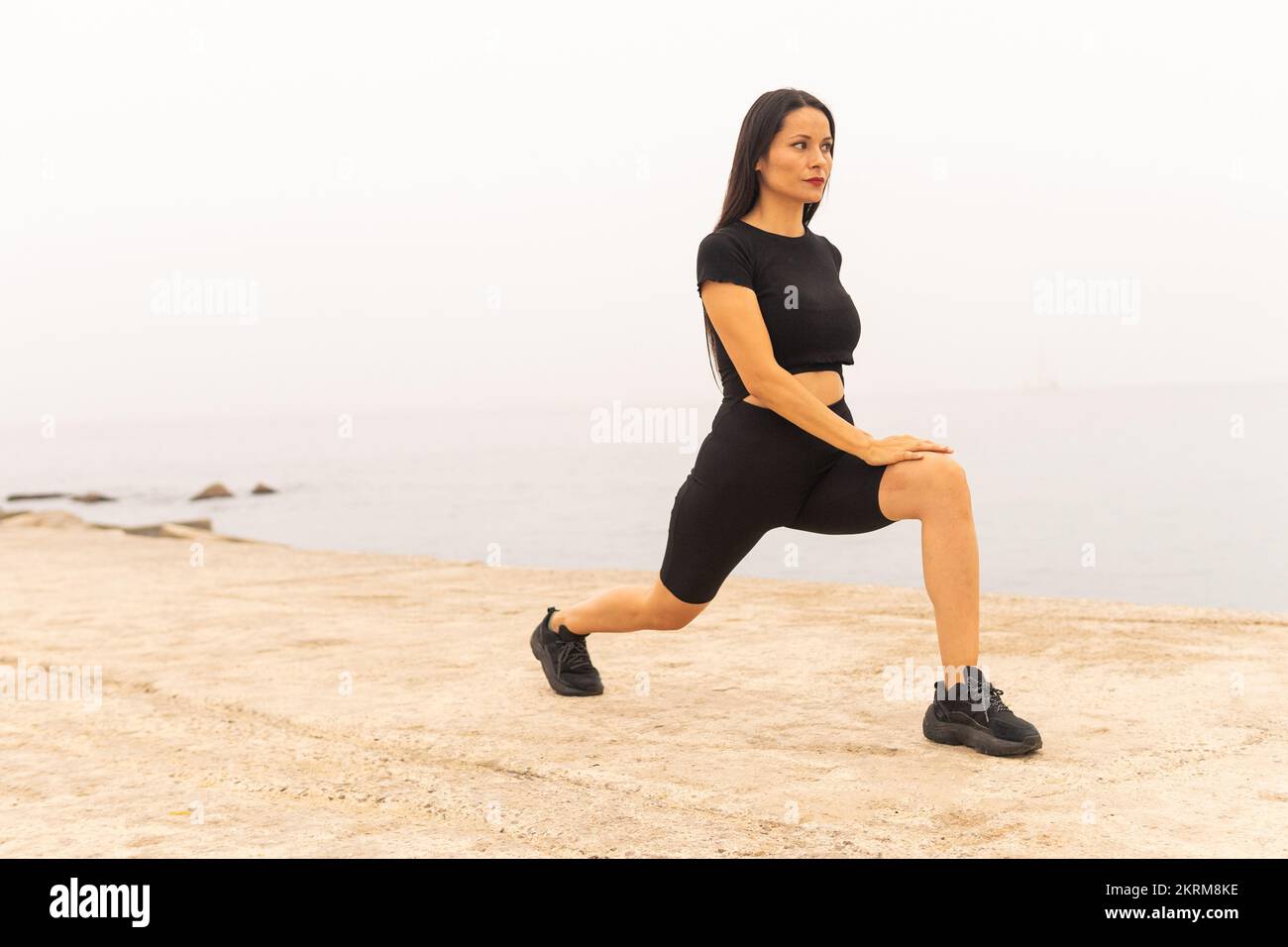 Full body of young sporty woman in black activewear stretching legs ...