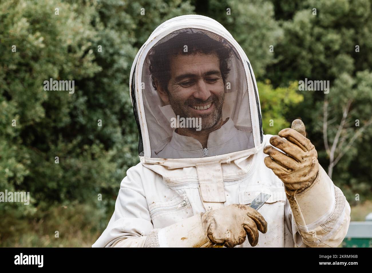 Smiling happy male beekeeper in white protective uniform and gloves ...